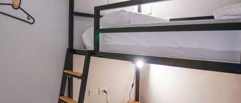 Quarto com beliche, escada, luminária na parede e tomada.