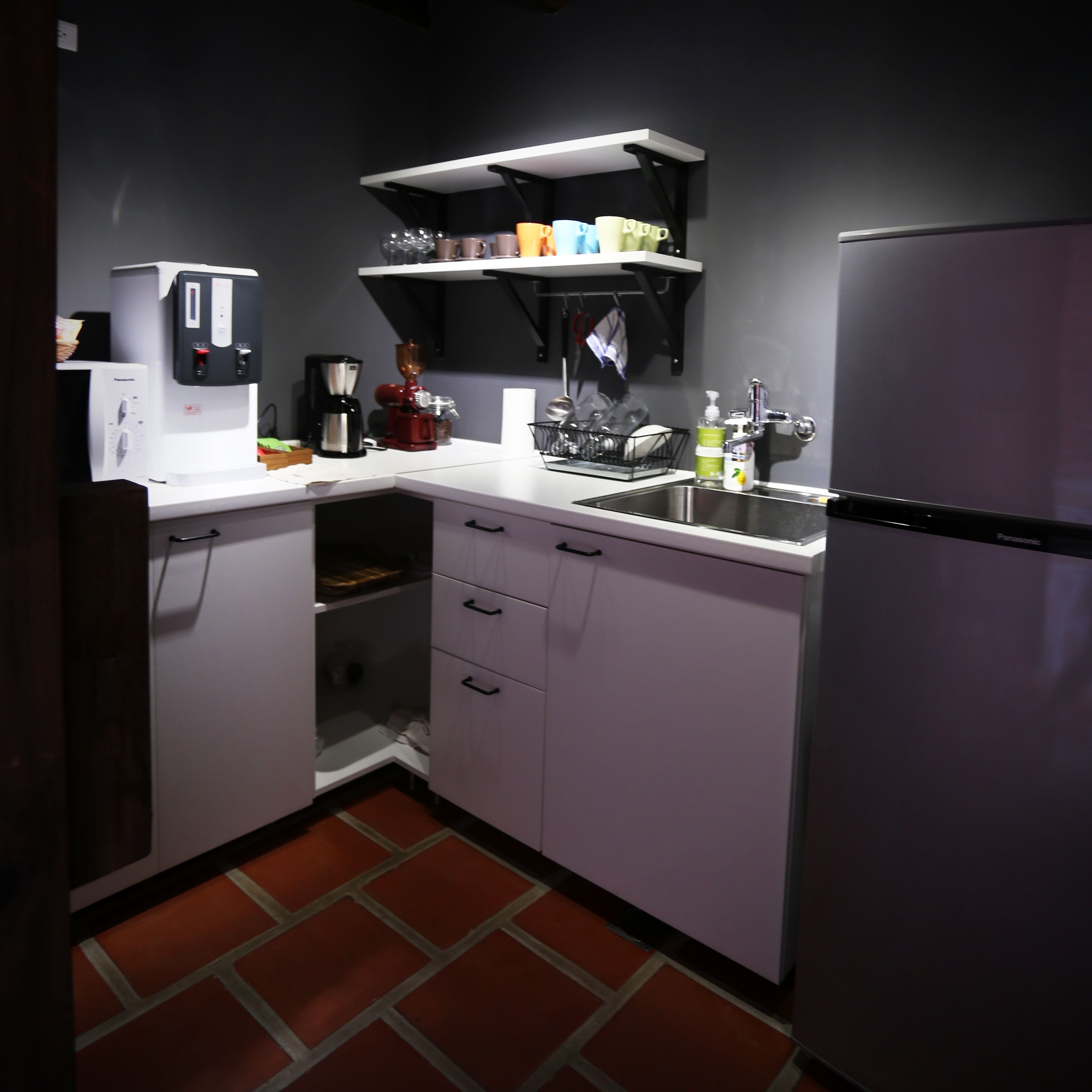 Uma cozinha compacta com armários brancos, pia embutida, geladeira e cafeteira.