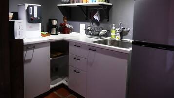 Uma cozinha compacta com armários brancos, pia embutida, geladeira e cafeteira.