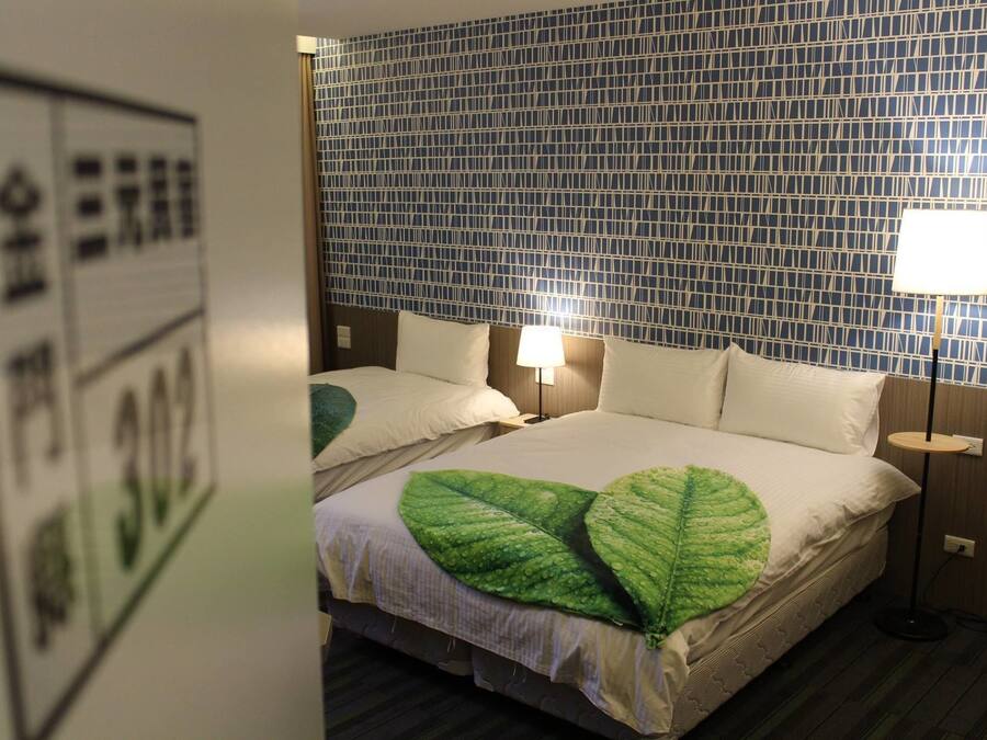 Quarto de hotel com duas camas, parede com padrão azul e branco e travesseiro em formato de folha verde.
