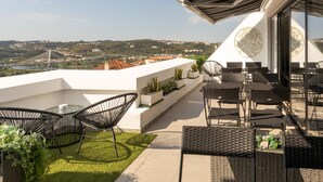 Terraço no telhado com área de estar ao ar livre, vista de uma ponte e área ajardinada com plantas.