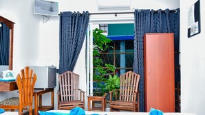 Quarto de hotel com uma cama, duas cadeiras de madeira, uma mesinha, uma televisão e um guarda-roupa.
