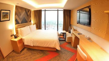 Quarto de hotel com uma cama grande, uma escrivaninha, uma televisão e vista para a cidade.