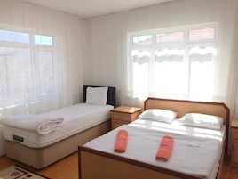 Quarto com duas camas, cabeceira de madeira, mesa de cabeceira e janela com cortinas.