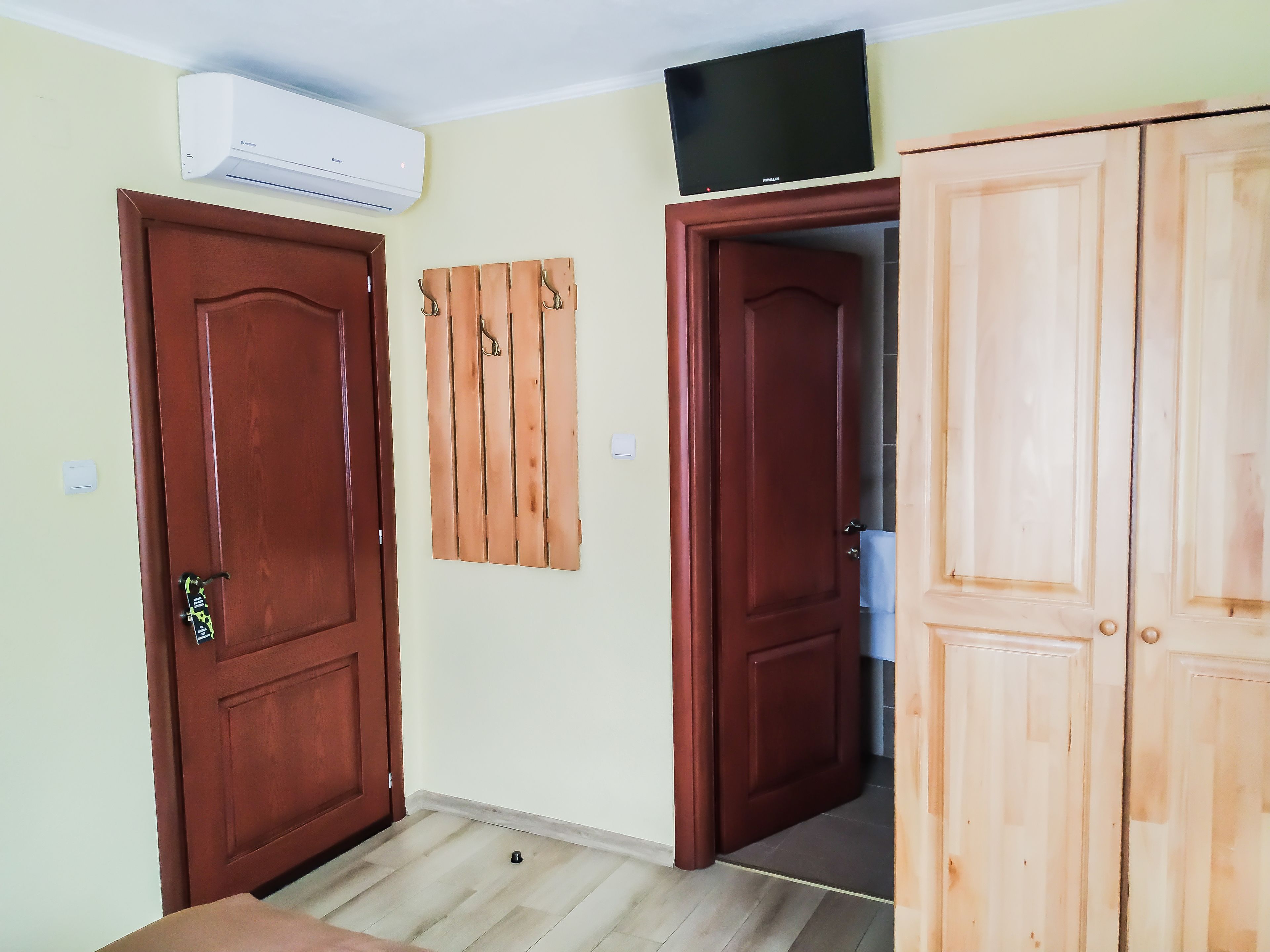 Quarto com duas portas de madeira, uma delas aberta, revelando um banheiro com parede azulejada e uma toalha pendurada. Um aparelho de ar condicionado está fixado na parede acima da porta à esquerda.