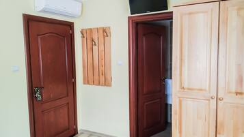 Quarto com duas portas de madeira, uma delas aberta, revelando um banheiro com parede azulejada e uma toalha pendurada. Um aparelho de ar condicionado está fixado na parede acima da porta à esquerda.
