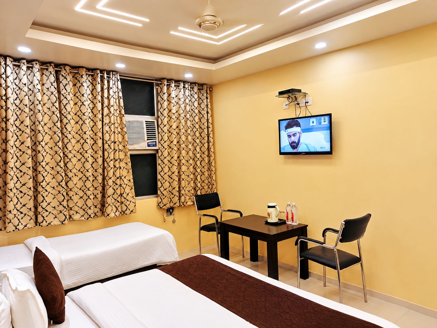 Quarto de hotel com duas camas, uma escrivaninha, uma cadeira, uma televisão e um ar condicionado.