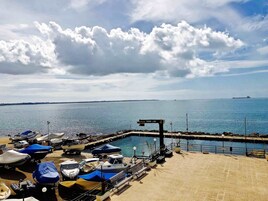 Marina com barcos atracados, uma plataforma de observação e vista ampla do mar e de um navio ao longe.