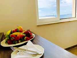 Uma tábua de frutas sobre a mesa, com vista para o mar pela janela.