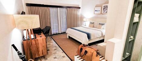 Quarto de hotel com cama, escrivaninha, cadeira, abajur e mala.