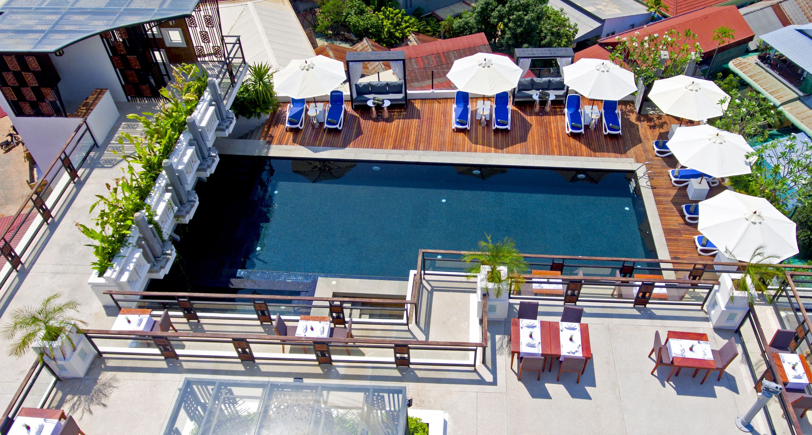 Vista aérea de uma área de piscina no terraço, com espreguiçadeiras e guarda-sóis, cercada por um deck de madeira e um parapeito de vidro.