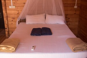 Quarto de cabana de madeira com cama, duas almofadas, mosquiteiro e toalhas.