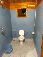 Um banheiro pequeno com vaso sanitário, um balde azul e chuveiro.