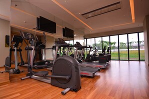 Academia com máquinas de cardio, televisão e amplas janelas.