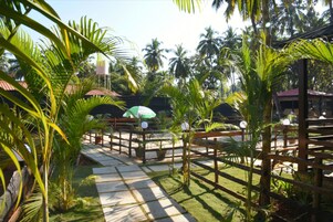 Um jardim tropical com palmeiras, cerca de madeira e um caminho.
