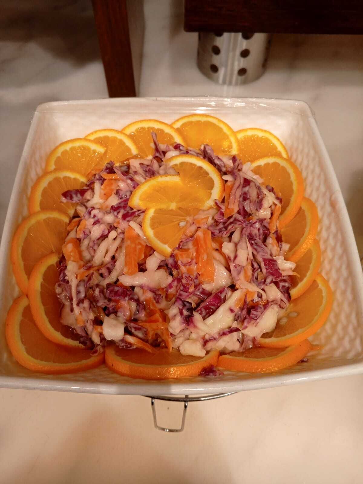 Uma tigela retangular branca com salada de repolho coberta com fatias de laranja, sobre uma superfície branca.