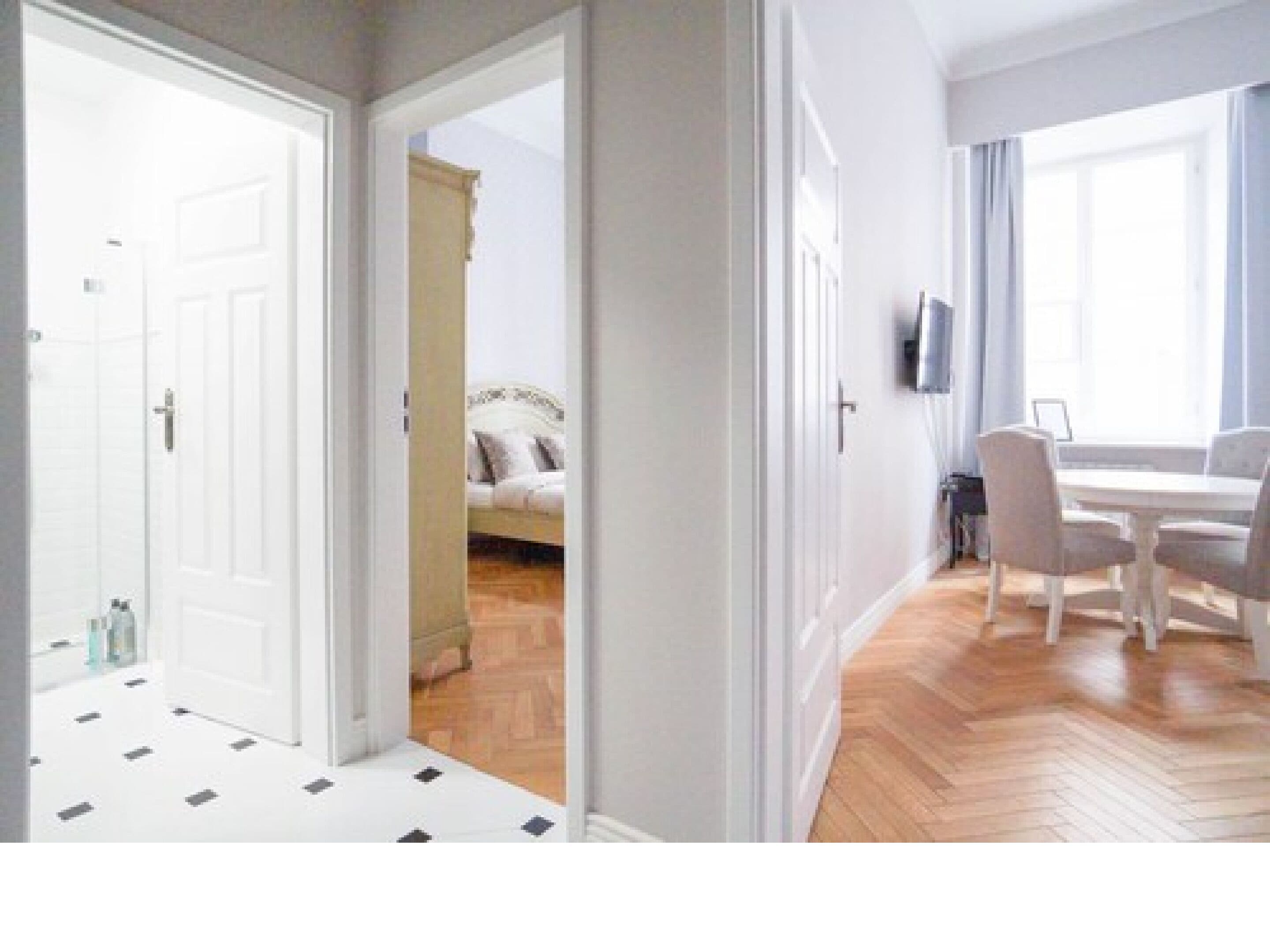 Quarto de hotel moderno com piso de madeira, uma cama, área de refeições com mesa e cadeiras, e uma TV fixada na parede.