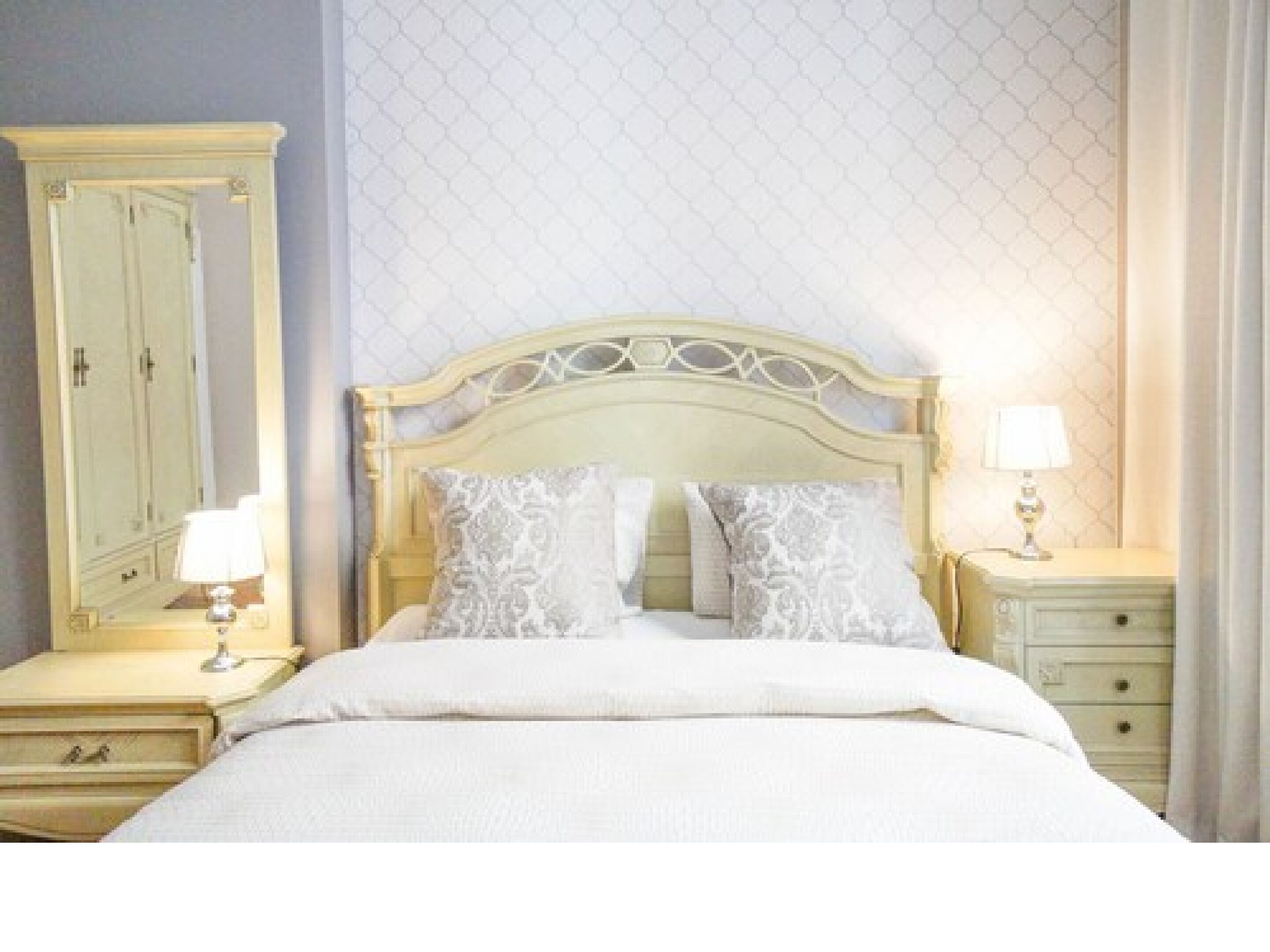 Cama bem arrumada com cabeceira, duas mesas de cabeceira com abajures e um guarda-roupa.