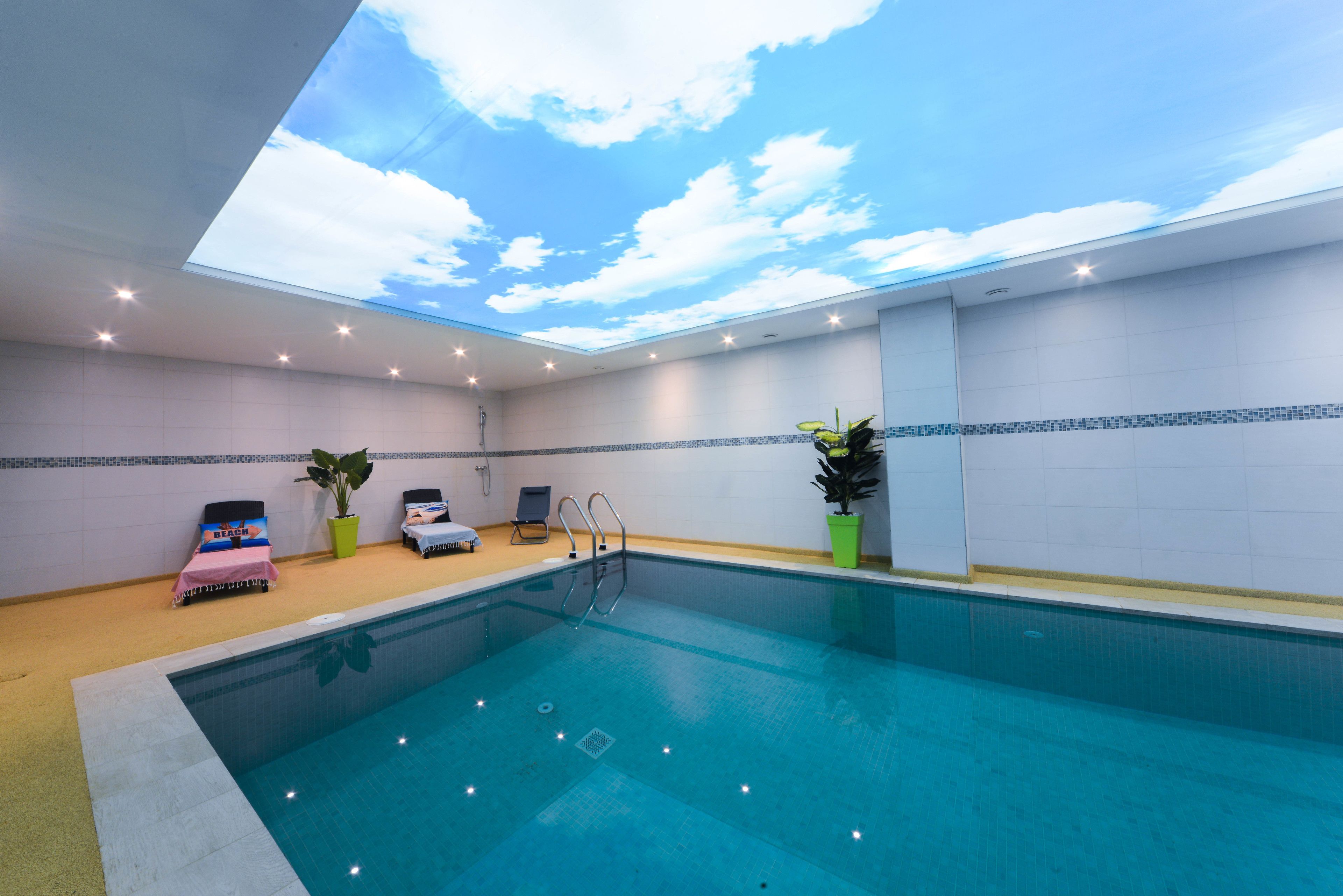 Uma piscina interior com teto skylight, duas espreguiçadeiras e plantas em vasos.