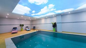 Uma piscina interior com teto skylight, duas espreguiçadeiras e plantas em vasos.