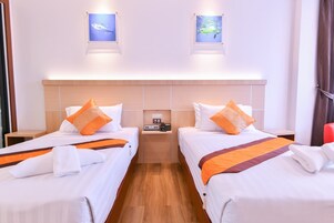 Quarto de hotel com duas camas, cada uma com roupa de cama branca e detalhes em laranja, uma cabeceira de madeira e uma mesa de cabeceira com telefone.
