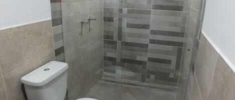 Uma casa de banho pequena e moderna com sanita, cabine de duche e rolo de papel higiénico.