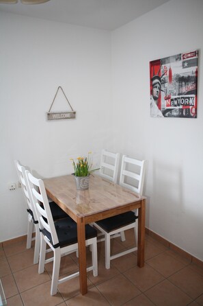 Uma mesa de jantar com quatro cadeiras brancas, um letreiro de boas-vindas e um pôster com vista para a cidade na parede.