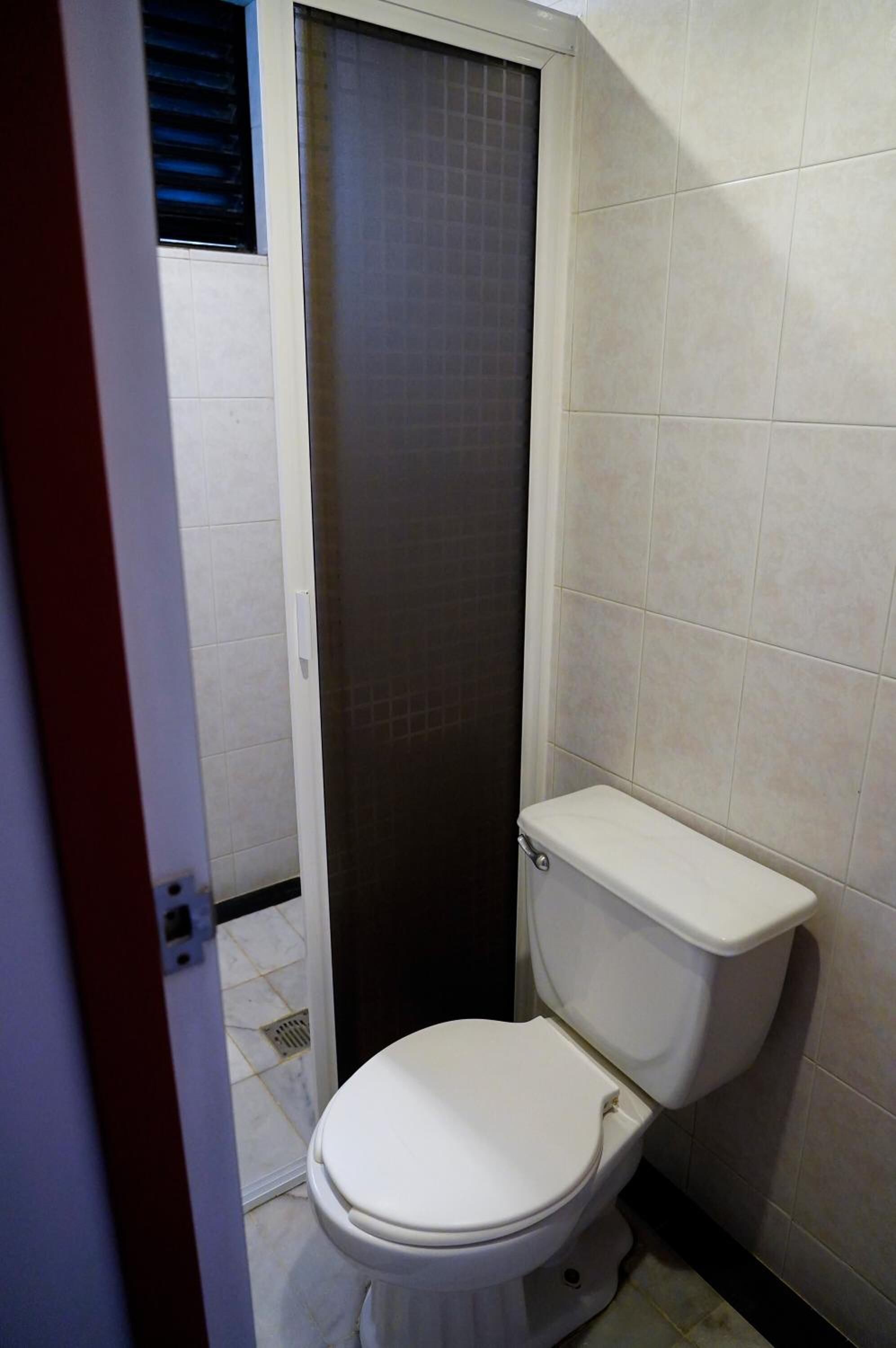 Casa de banho pequena e compacta, com sanita branca, área de duche revestida a azulejos e porta que dá para outro espaço.