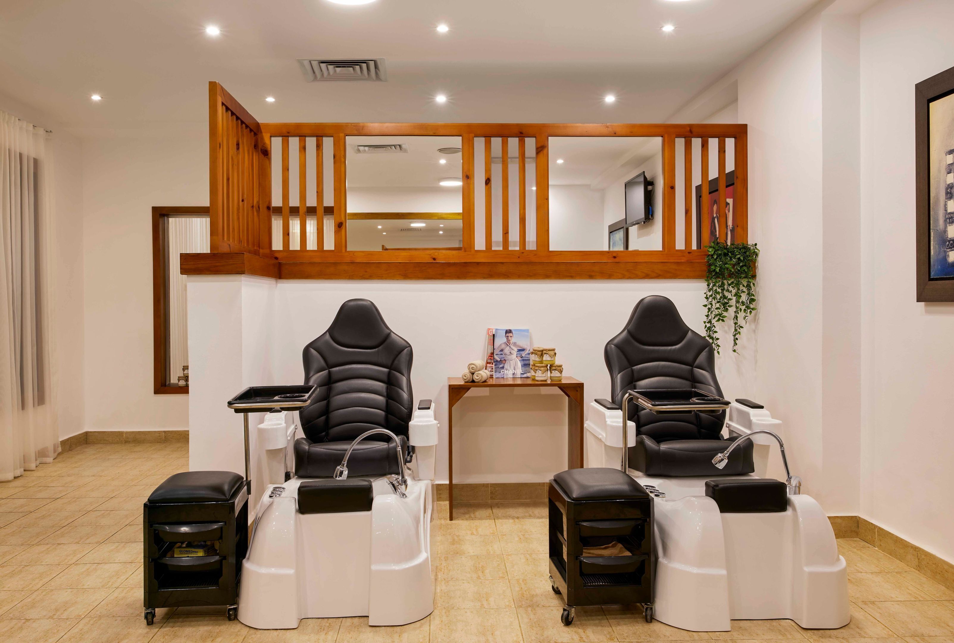 Um quarto com duas cadeiras de massagem, uma mesinha com revistas e um espelho sobre as cadeiras.