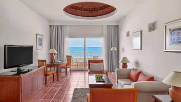 Quarto de hotel com televisão, área de estar e varanda com vista para o mar.