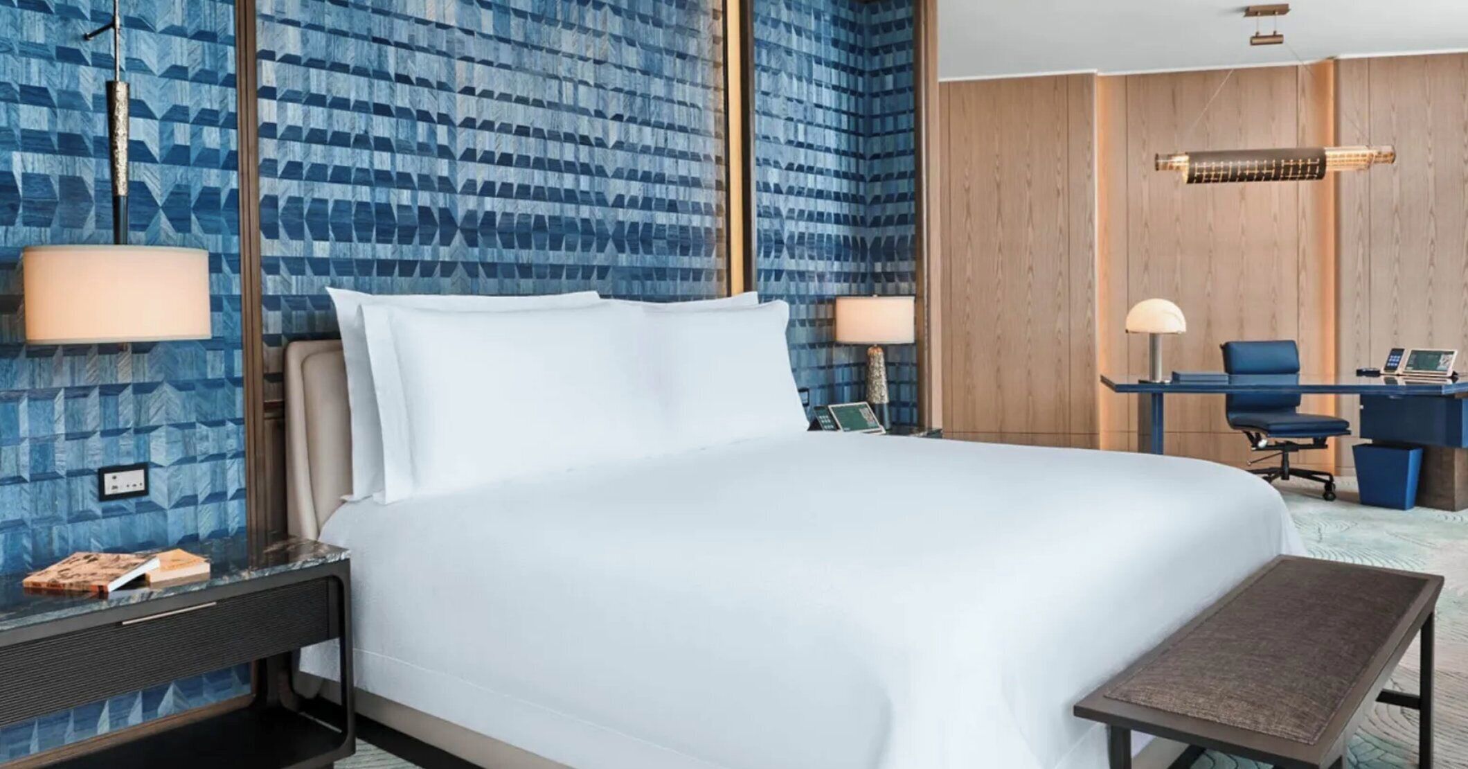 Quarto de hotel com uma cama grande, mesas de cabeceira, escrivaninha e uma cadeira.