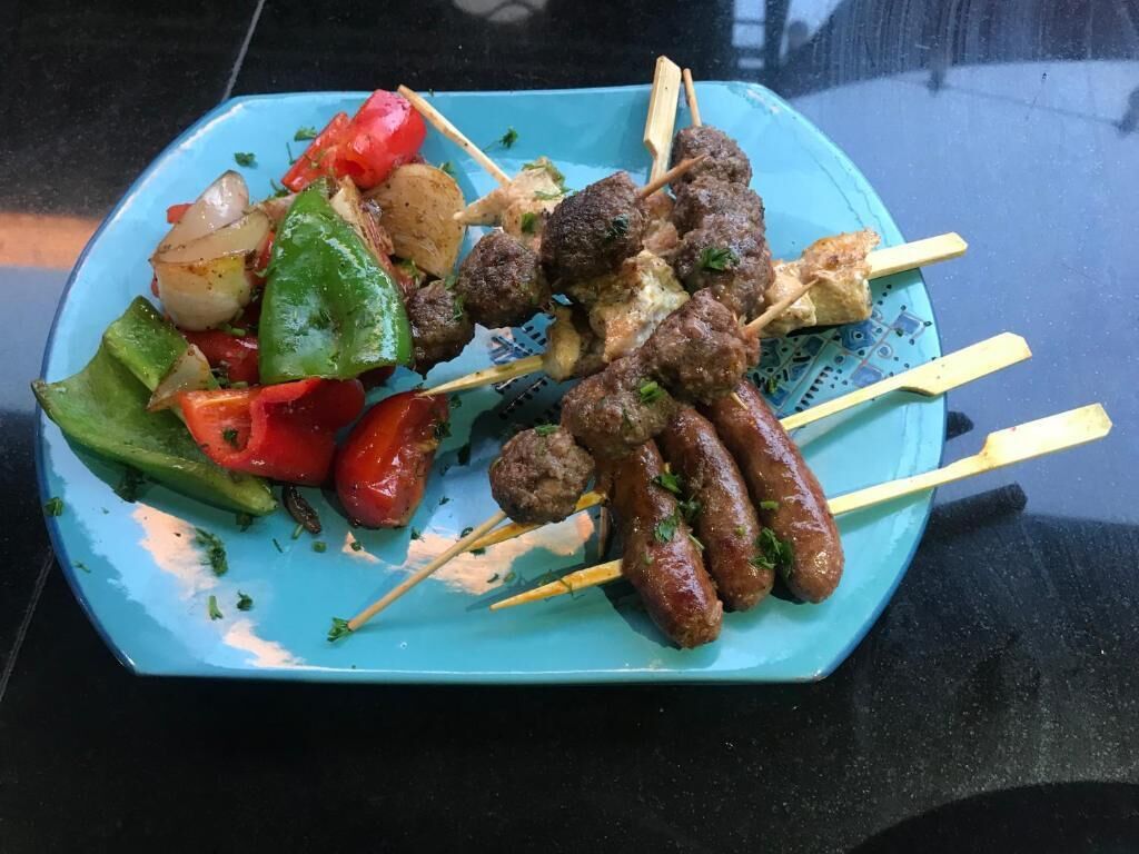Um prato azul com espetinhos de carne, legumes e uma salada.