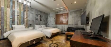 Quarto de hotel moderno com duas camas, uma escrivaninha com computador, televisão de tela plana e um painel decorativo na parede.