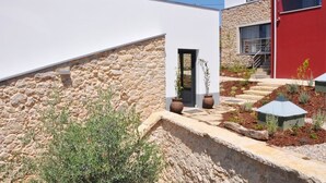 Um edifício moderno com fachada de pedra, parede externa vermelha e pequena entrada com plantas em vasos.