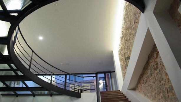 Um interior moderno com escada em espiral, parede de pedra e guarda-corpo de vidro.