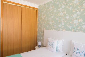 Quarto com cama, almofadas, mesa de cabeceira e guarda-roupa de madeira.