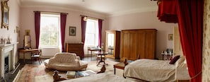 Quarto com lareira, sofá, cama, guarda-roupa de madeira e mesa com um vaso de flores.