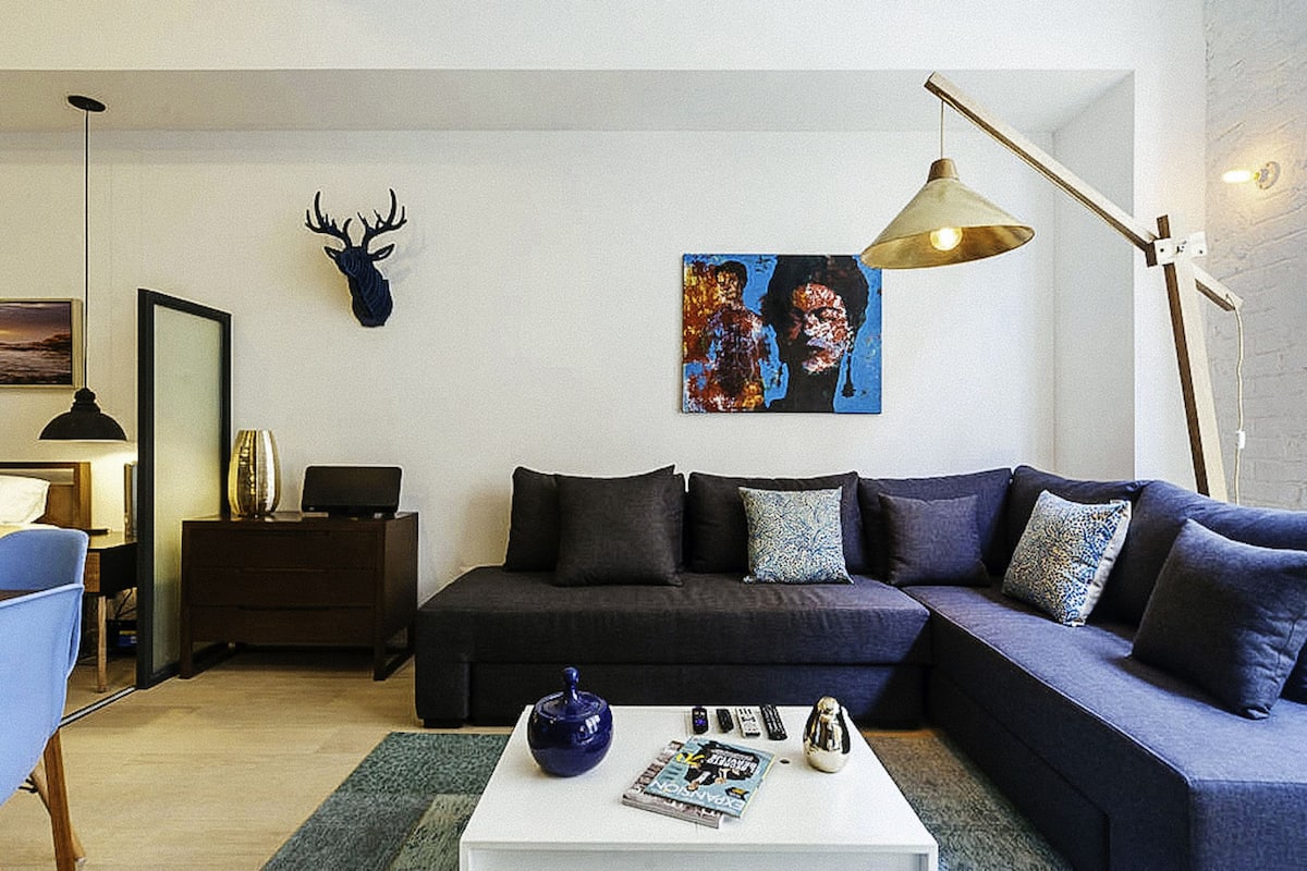 Uma sala de estar moderna com um sofá escuro, uma mesa de centro branca e um quadro na parede.
