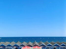 Fileira de cabanas de praia com vista ampla para o mar e alguns gaivotas empoleiradas nos telhados.