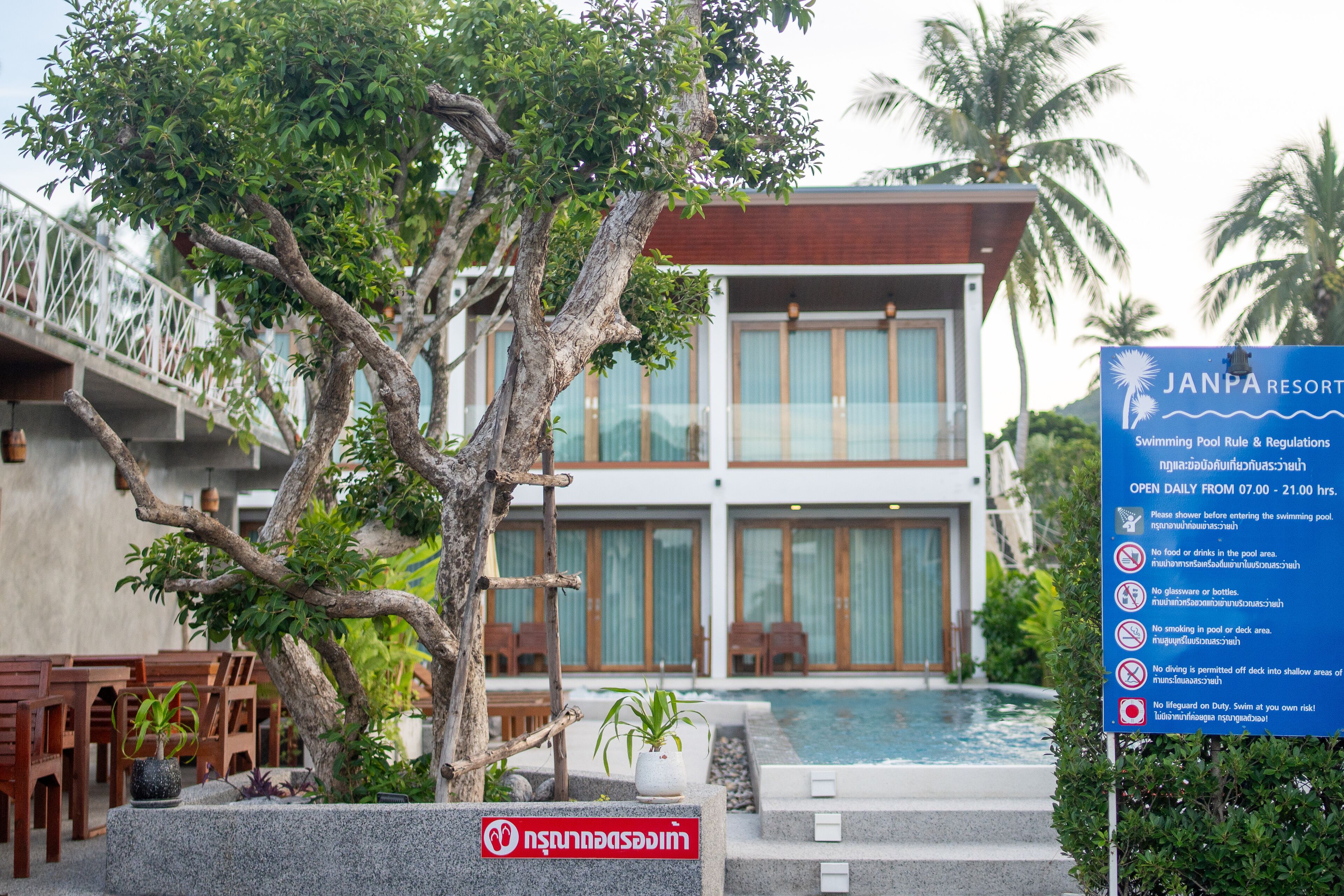 Um resort com piscina, uma placa de avisos e uma árvore ao primeiro plano.