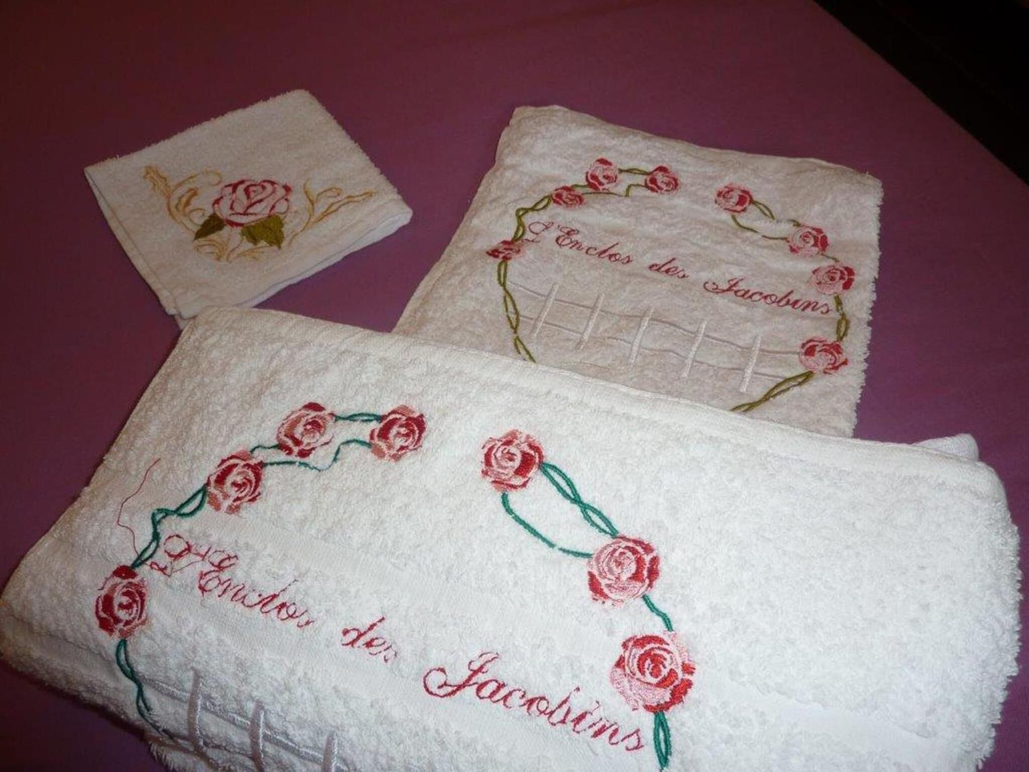 Três toalhas brancas com bordados de rosas e texto.