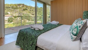 Quarto com uma cama grande, varanda com vista para áreas verdes e edifícios, e parede de painel de madeira.