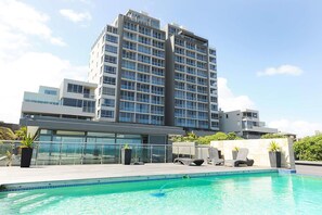 Um hotel moderno com piscina no terraço, janelas amplas e um edifício alto ao fundo.