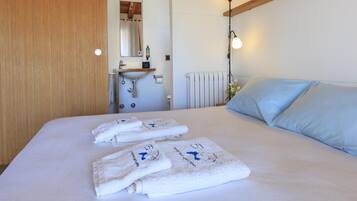 Quarto de hotel com cama, mesa de cabeceira, abajur, espelho e banheiro visível por uma porta aberta.
