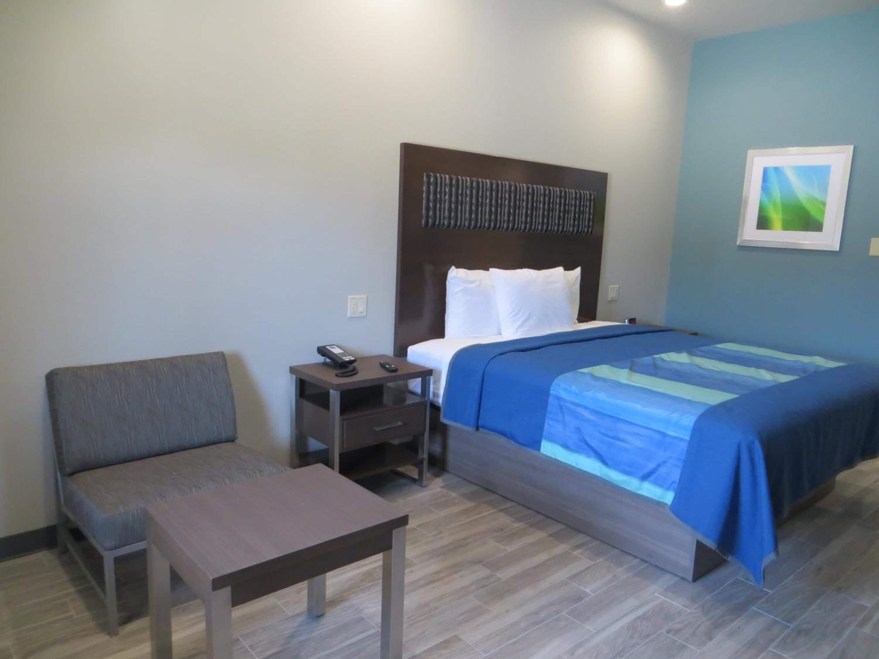 Quarto de hotel com cama, mesa de cabeceira, cadeira e uma pequena mesa.