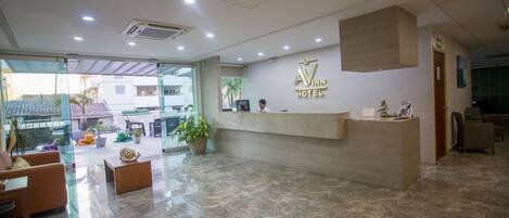 Uma área de recepção de hotel com piso de mármore, balcão de recepção e vista para o exterior.