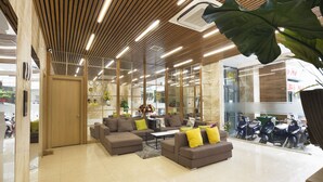Um lobby moderno com teto de madeira, área de estar com sofás e mesa de centro, e uma planta grande.