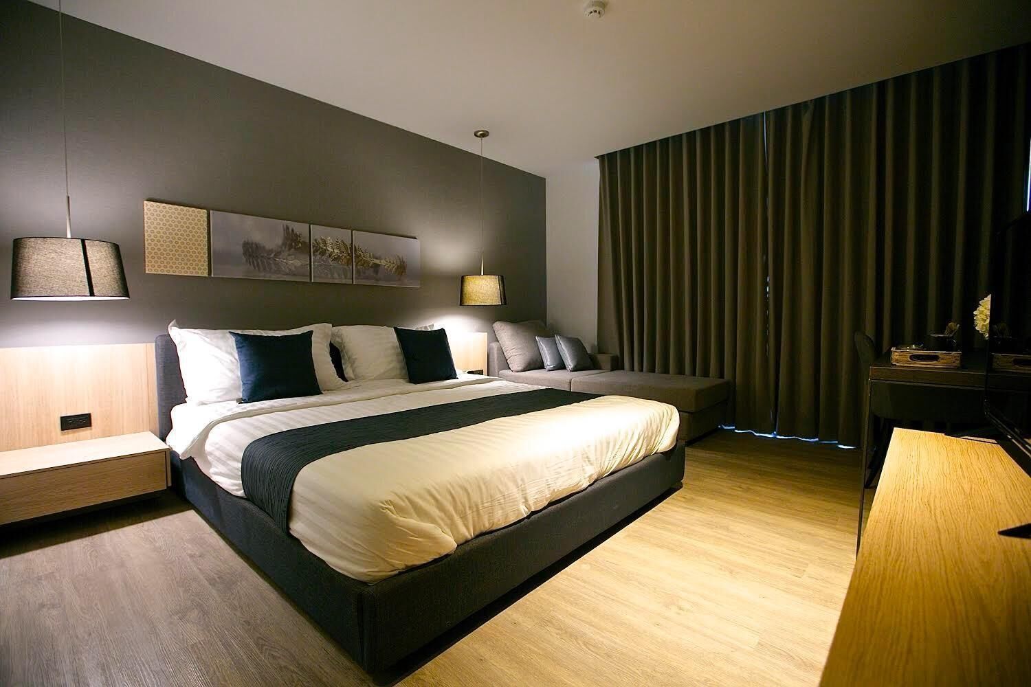 Quarto de hotel moderno com uma cama grande, mesas de cabeceira, uma escrivaninha e vista para a cidade.