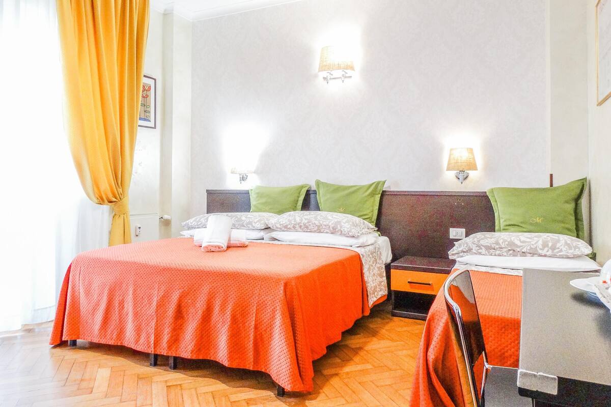 Quarto de hotel com duas camas, cada uma com cabeceira, e uma pequena mesa.