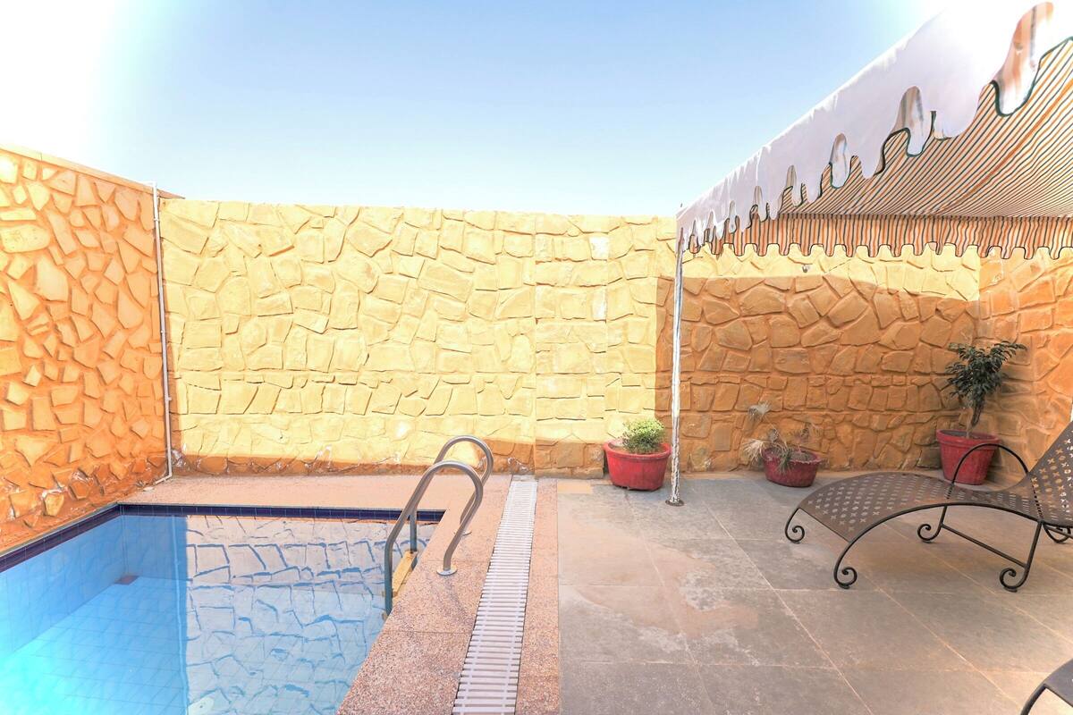 Piscina ao ar livre com paredes de pedra e uma cadeira de metal.